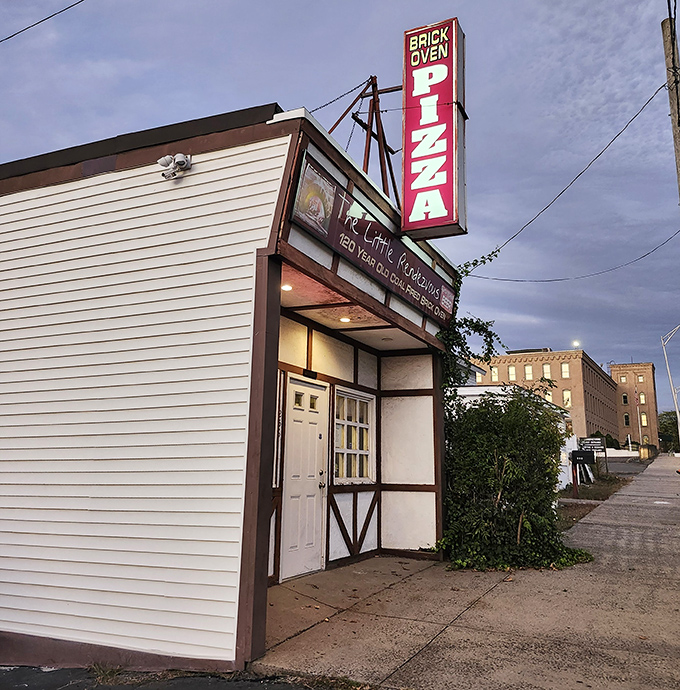 The humble exterior of Little Rendezvous conceals pizza history inside. That doorway leads to a flavor time machine powered by coal and tradition.