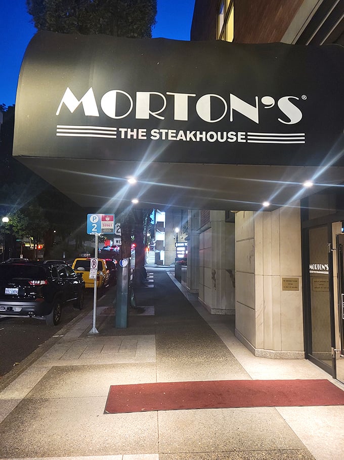 Soft lights shine from Morton’s The Steakhouse awning while cars line the quiet street beside it.