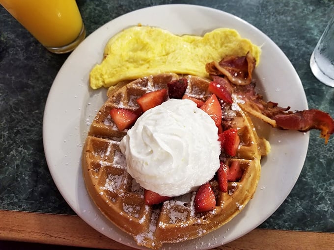 A Belgian waffle crowned with whipped cream and strawberries sits alongside eggs&mdash;breakfast royalty holding court with its loyal subjects.