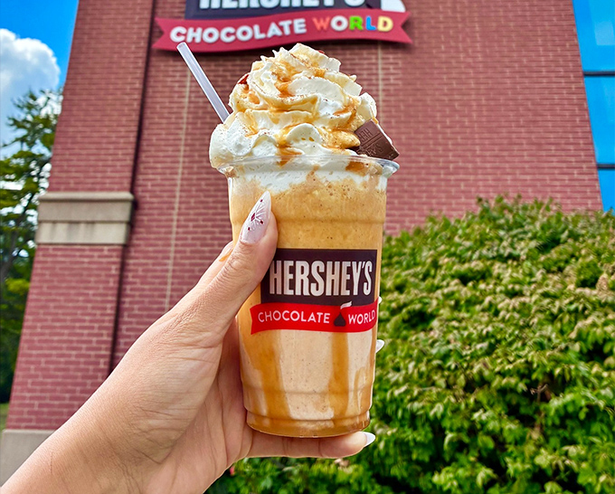 A caramel-topped milkshake that's basically wearing a crown of whipped cream, standing proudly against the Hershey's Chocolate World backdrop.