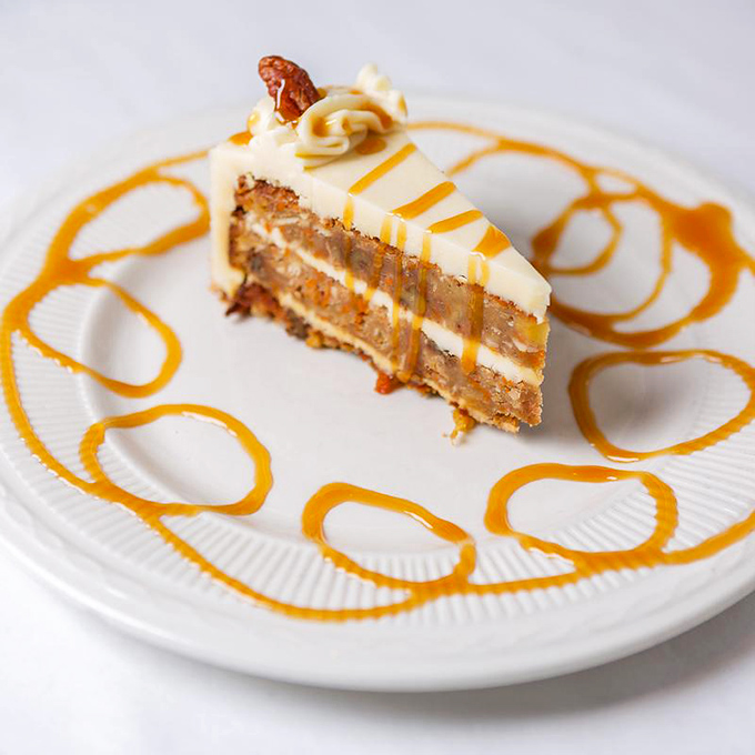 Layered carrot cake with cream cheese frosting and caramel drizzle offers a delightful alternative to traditional Italian desserts at TAT.