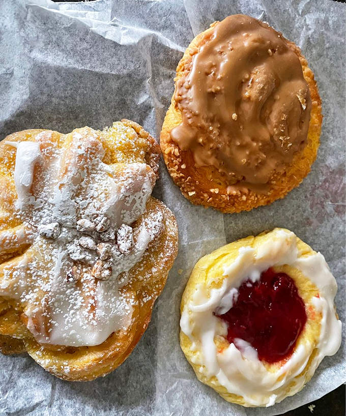 Glazed Danish pastries glistening under bakery lights like they're auditioning for a starring role in your breakfast dreams.