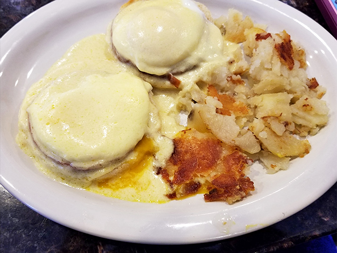 Eggs Benedict done right &ndash; hollandaise cascading down like a yellow waterfall of buttery goodness. The home fries look like they've been kissed by the griddle gods.
