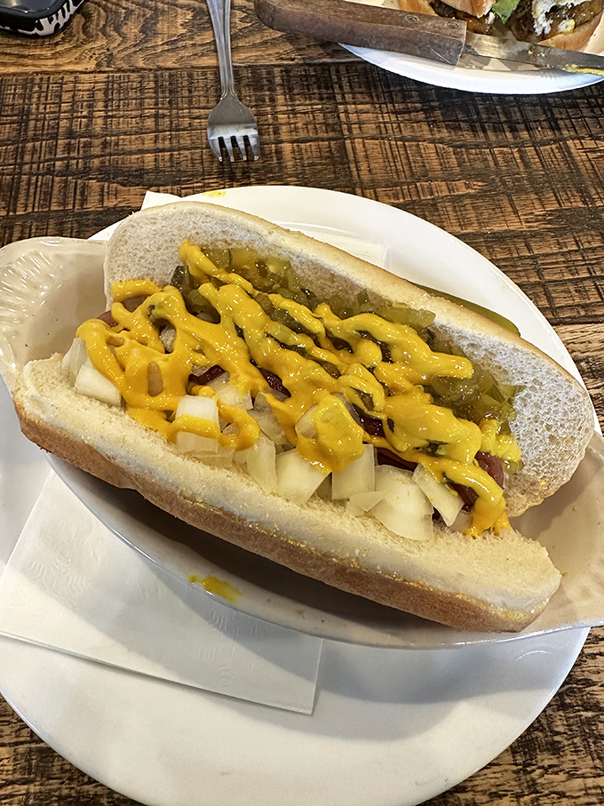 The hot dog reimagined as royalty. Yellow mustard drizzled like edible sunshine over a symphony of toppings that elevate the humble frank.