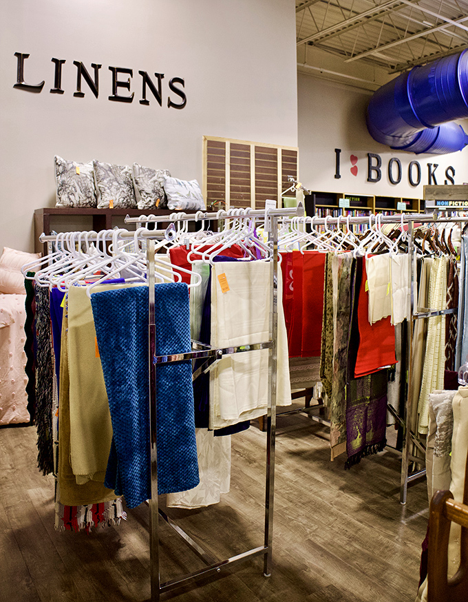 The linens section: where tablecloths, napkins, and scarves hang like colorful flags representing the Republic of Incredible Bargains.