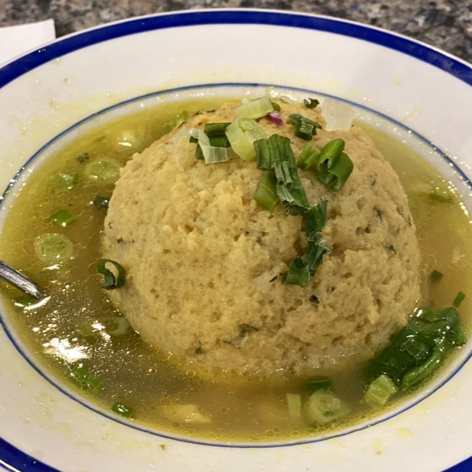 This matzo ball soup isn't just comfort food—it's a warm hug in a bowl, with a dumpling island floating in golden broth paradise.