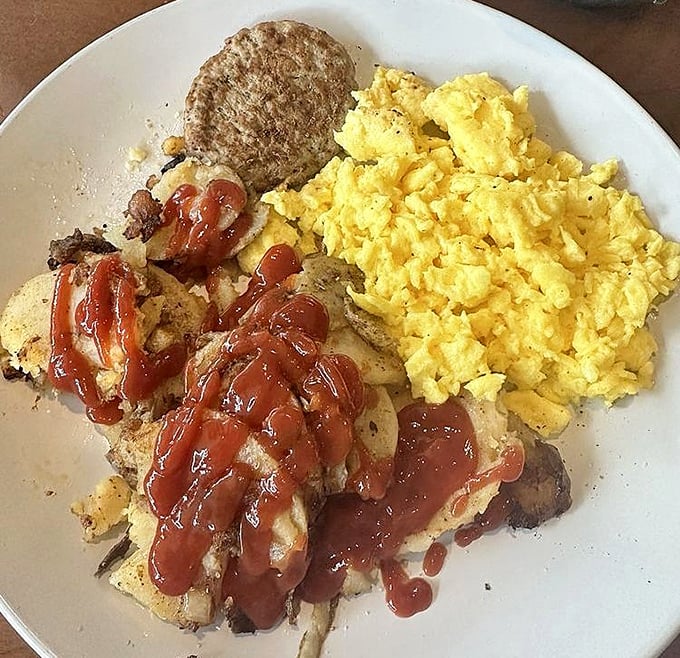 Breakfast alchemy at its finest—fluffy scrambled eggs, crispy potatoes, and that zigzag of sauce that transforms simple ingredients into morning magic.