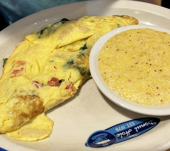 This isn't just an omelet; it's a golden envelope delivering a message of breakfast perfection alongside creamy grits that whisper "good morning" in a Southern accent.