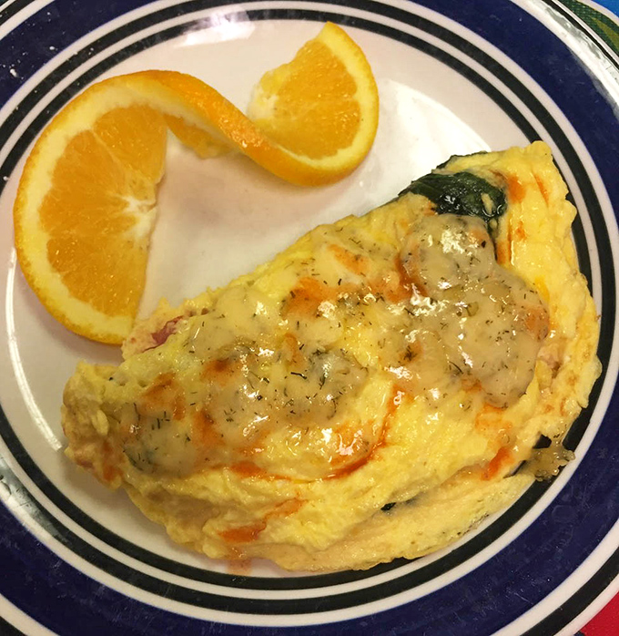 A fluffy omelet paired with fresh orange slices proves that balance exists, even when you're eating your weight in cheese.