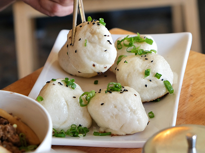 Pan-fried pork buns wear their sesame seeds and scallions like fancy hats, golden bottoms peeking out.