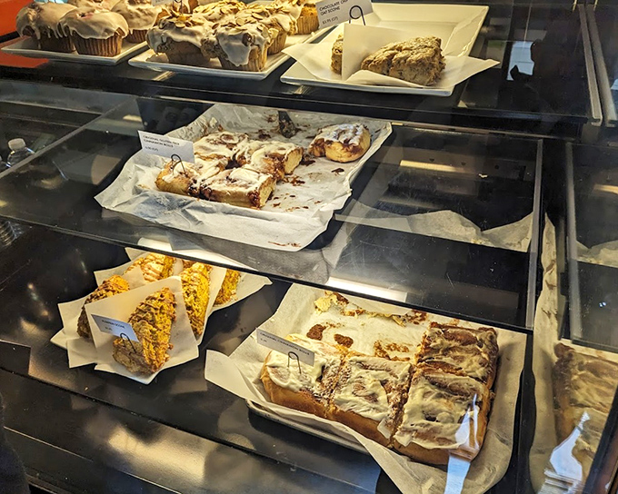 The display case—where pastry dreams are born and diets go to die. Each tray offers a different path to happiness, all equally justified.
