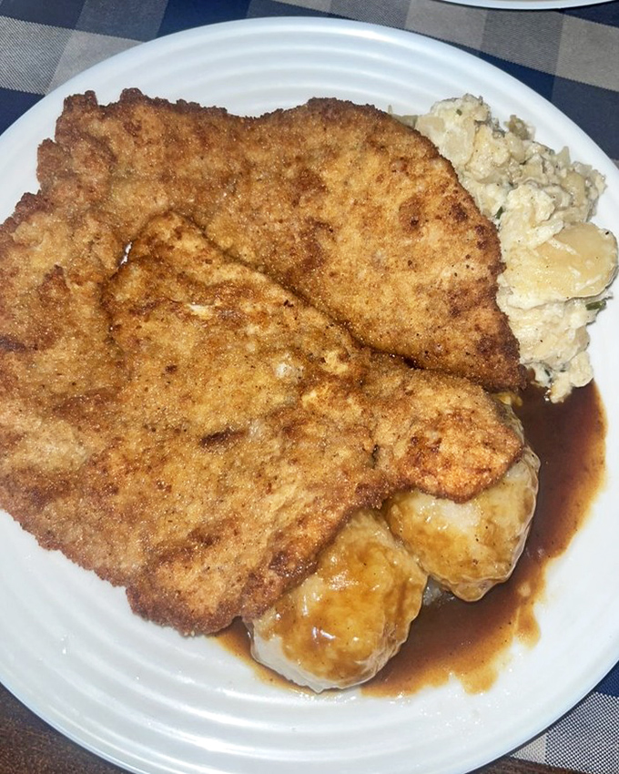 This magnificent pork schnitzel stretches across the plate like golden, crispy perfection, complete with potato dumplings and rich gravy.