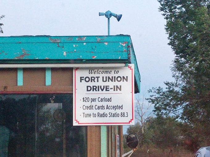 The weathered metal snack bar glows like a lighthouse in the desert night, beckoning moviegoers with promises of buttery popcorn and cold drinks.