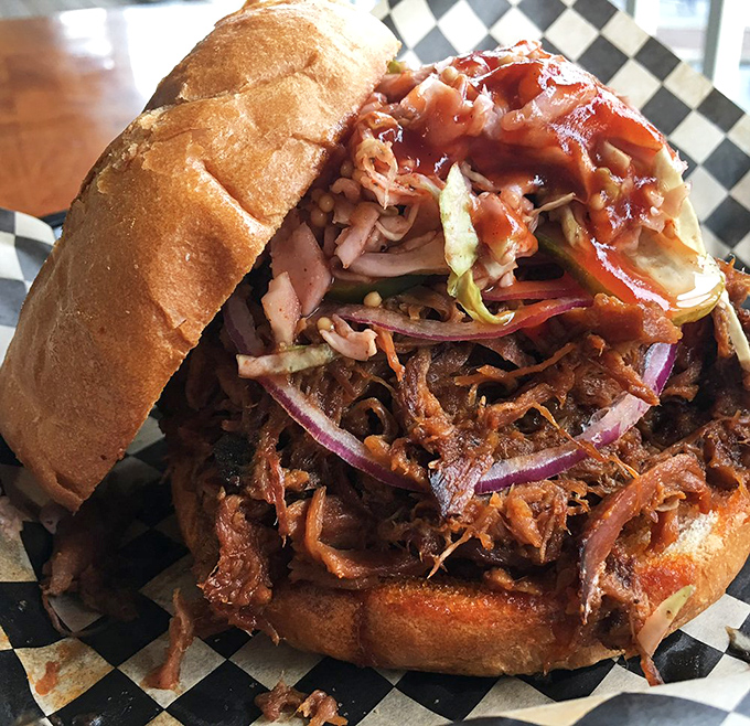 The pulled pork sandwich arrives like a savory volcano, with tender meat erupting from a toasted bun and topped with a colorful slaw avalanche.