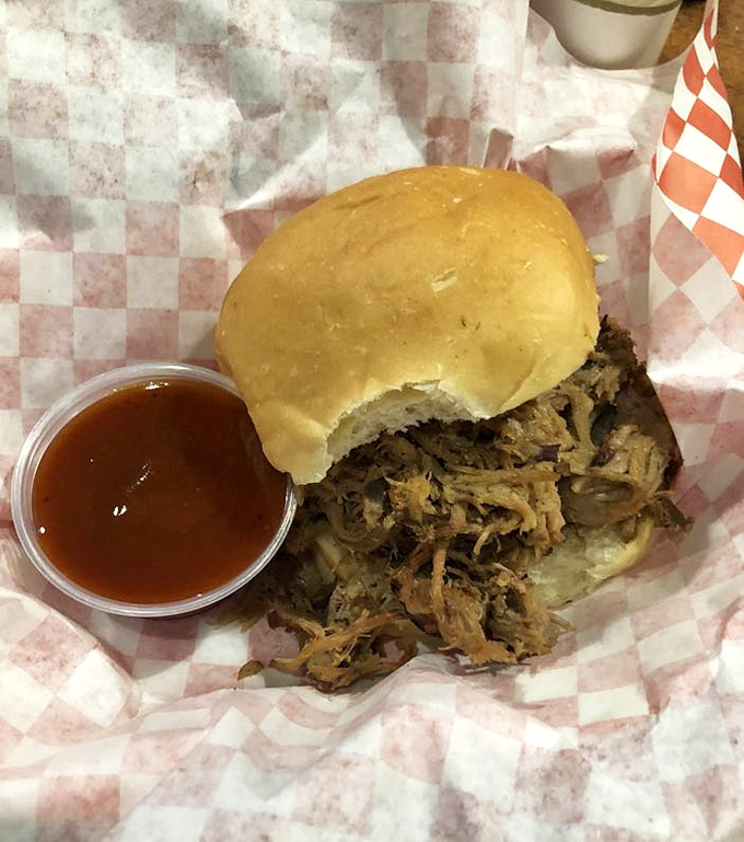 The pulled pork sandwich in its natural habitat: checkered paper, simple bun, sauce on the side. Barbecue minimalism at its finest. 
