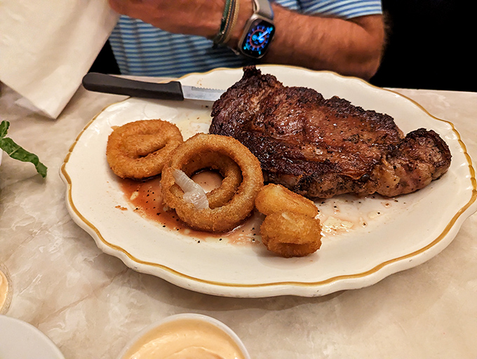 A ribeye that's been introduced to heat with proper respect, accompanied by golden onion rings. This isn't just dinner&mdash;it's a celebration on a plate.