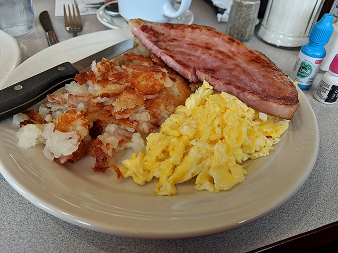 Behold the breakfast of champions! Fluffy scrambled eggs, a ham slice thick enough to make a statement, and hash browns that crackle with each forkful.