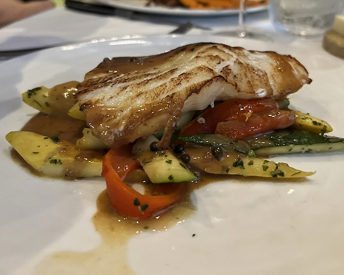 Perfectly seared sea bass rests atop a colorful medley of vegetables &ndash; proof that sometimes the simplest preparations yield the most spectacular results.