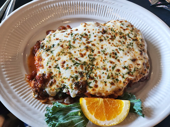 Beneath that golden blanket of melted cheese lies a dish that would make any Italian grandmother nod in approval. The orange wedge adds a pop of color and freshness. 