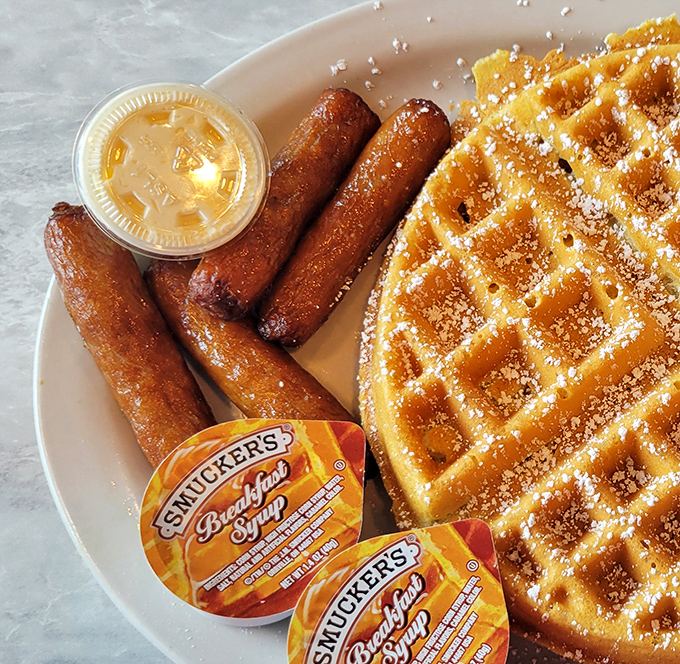 Golden waffle perfection meets sausage links in a breakfast symphony. Those Smucker's syrup packets are the backup singers to this morning masterpiece.