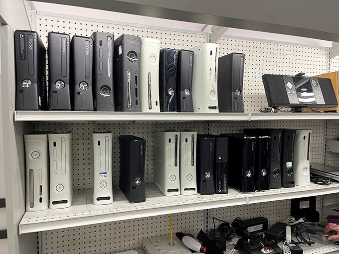 Gaming history displayed on pegboard! From original Xboxes to PlayStation classics, this tech graveyard is a collector's gold mine.