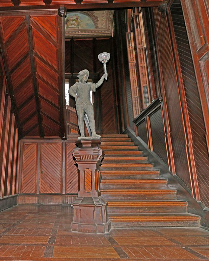 This grand wooden staircase has supported generations of footsteps. The statue seems to say, "Yes, I've been holding this lamp since before electricity."