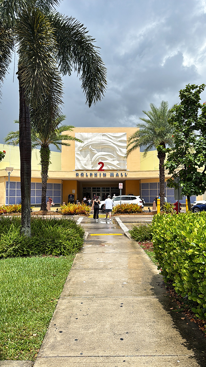 A palm-lined pathway leads to retail nirvana. The landscaping offers a quintessential Florida welcome before the air-conditioned shopping marathon begins.