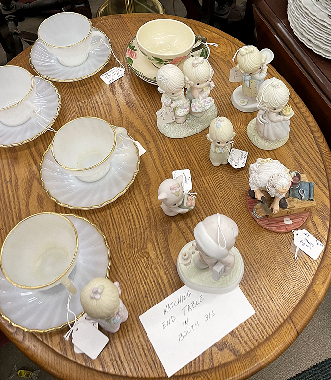 Precious Moments figurines stand guard over delicate teacups. These porcelain time travelers have survived decades without a single chip.