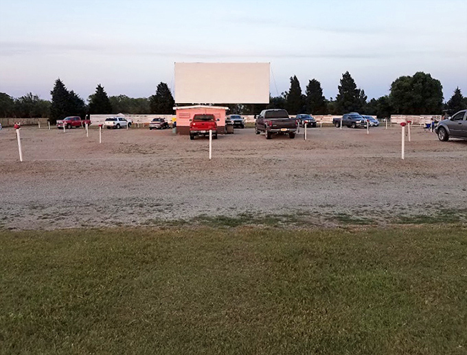 The parking lot fills as dusk approaches, each vehicle finding its place in this democratic theater where pickup trucks and sedans share equal viewing rights.