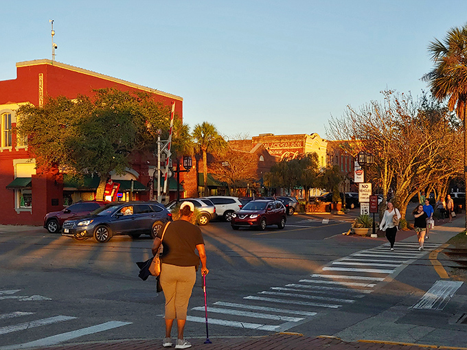 Golden hour light warms the historic brick buildings and the busy street corner, casting long shadows as pedestrians stroll through the heart of the downtown area.