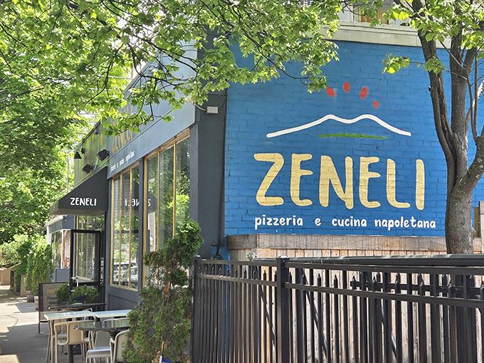 The bold blue wall of Zeneli announces "pizza artistry happens here." That outdoor seating area? Your personal box seat to the theater of Wooster Street.