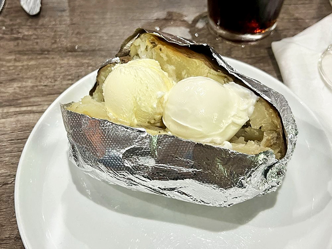 The humble baked potato, dressed in its aluminum tuxedo and crowned with scoops of butter, awaits its supporting role in the steak dinner symphony.