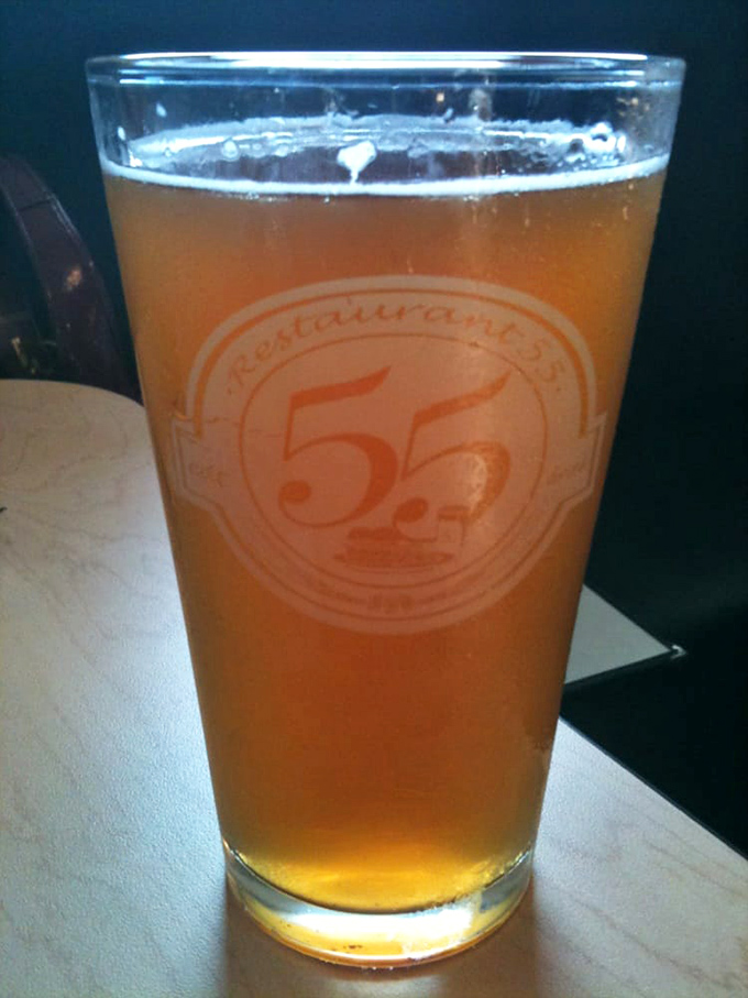 A golden glass of beer bearing the Restaurant 55 logo&mdash;because sometimes the perfect burger companion isn't a person, it's a pint.