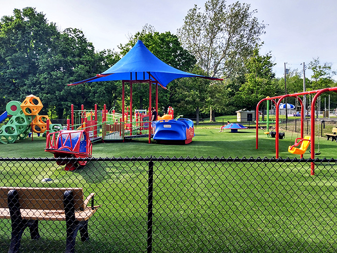 Primary colors and playground equipment under blue shade structures&mdash;where childhood happens at the perfect, unhurried pace.