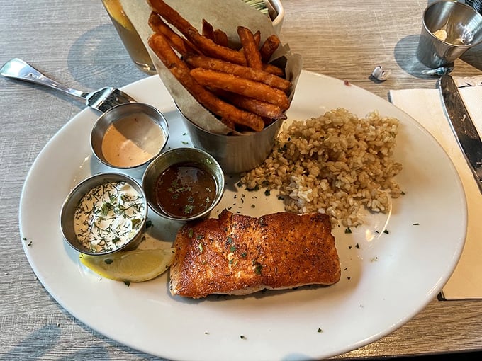 A perfectly seared salmon fillet accompanied by sweet potato fries and grain pilaf. The trio of dipping sauces proves that thoughtful details elevate a good meal to greatness.