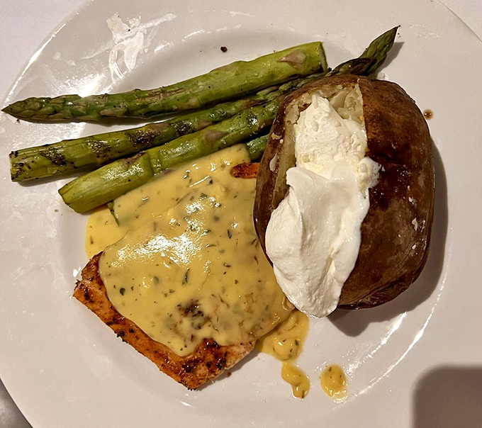 Salmon wearing a blanket of creamy sauce, accompanied by asparagus soldiers and a baked potato that's having an identity crisis with that dollop of cream.