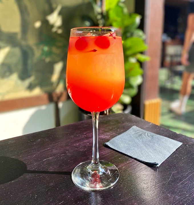 That sunrise-colored cocktail isn't just a drink – it's liquid sunshine in a glass, complete with cherries that look like they're having more fun than you are.