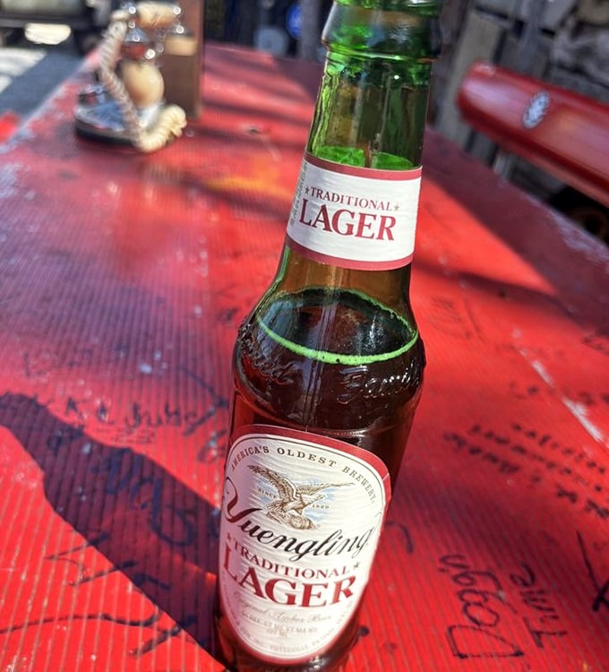 Nothing complements a hot dog feast like an ice-cold lager on a sun-dappled table. The graffiti underneath tells stories you wish you knew.