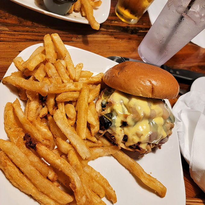 The burger arrives like a towering monument to beef perfection, with fries so golden they could fund your retirement plan.