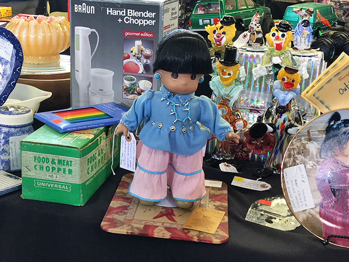 This vintage doll waits patiently among kitchen gadgets and colorful trinkets, silently judging your hesitation to adopt her into your home.