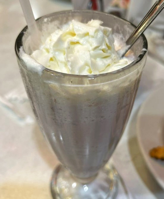 The milkshake arrives with whipped cream mountain peaks so high they deserve their own elevation markers. Spoon required, patience recommended.