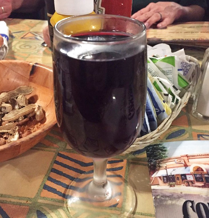 A glass of rich red wine stands ready to complement your meal, proving that even in casual surroundings, life's simple pleasures deserve proper respect.