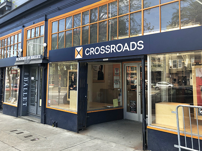Crossroads Trading's navy blue storefront sits elegantly between neighboring businesses. Those large windows showcase curated fashion finds within.