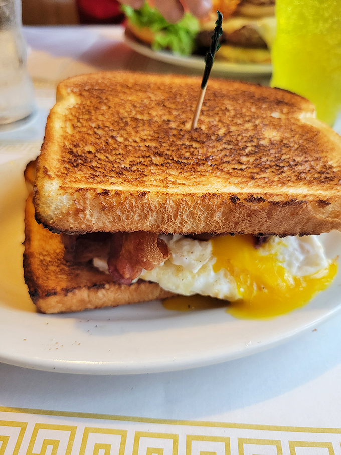 Breakfast sandwich perfection: golden toast, melty cheese, crispy bacon, and that glorious moment when you pierce the egg yolk. Poetry on a plate.
