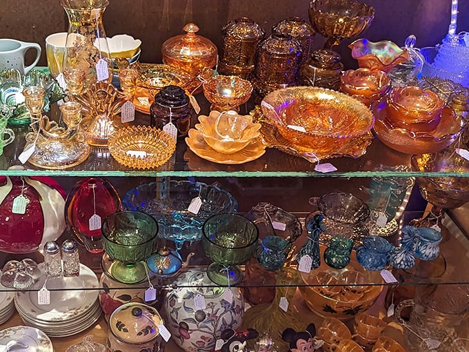 Amber carnival glass catches light like liquid honey, arranged in tiers of translucent treasure that collectors hunt with the fervor of gold prospectors.