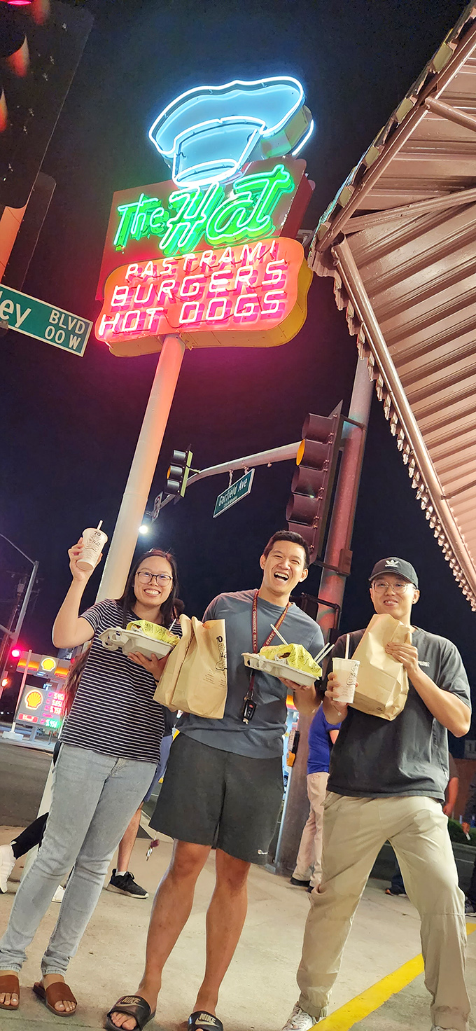 Night pilgrims at the neon altar of pastrami, clutching their treasures with the joy of true believers.