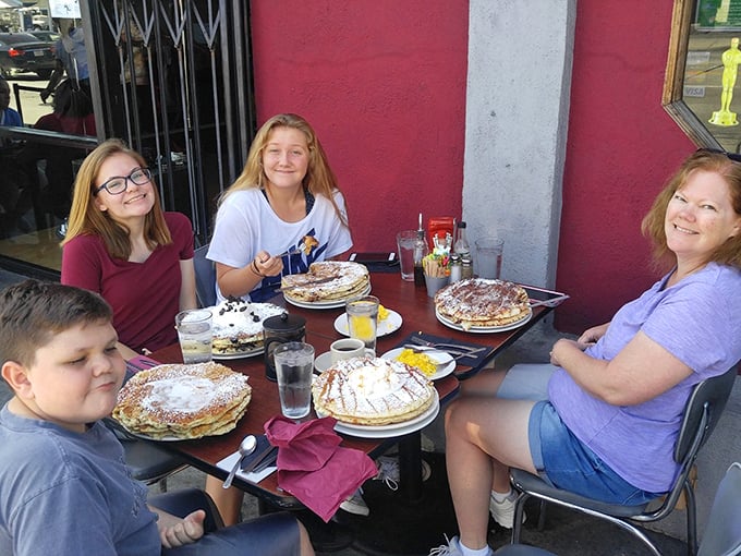 Family breakfast joy captured in its natural habitat. Those plate-sized pancakes have clearly created memories sweeter than the syrup they're soaked in.
