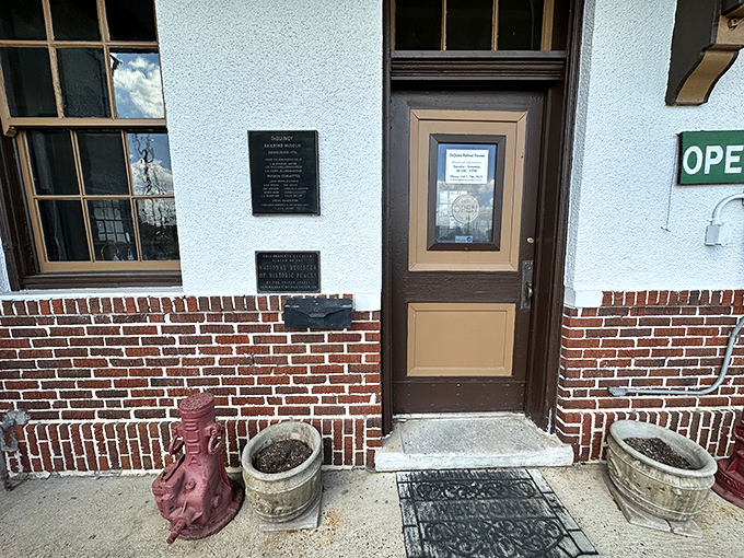 The entrance beckons with simple charm, flanked by planters and historical markers. That door has welcomed countless visitors seeking connection with America's railroad heritage.