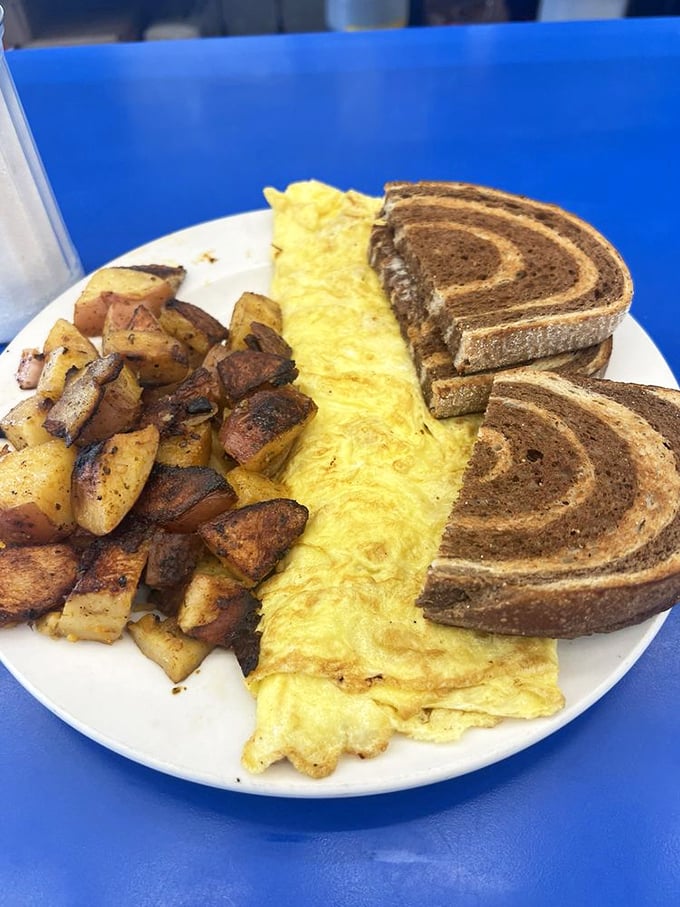 The perfect diner breakfast trifecta: a fluffy omelet, crispy-edged home fries, and marble rye toast&mdash;simple perfection on a white plate.