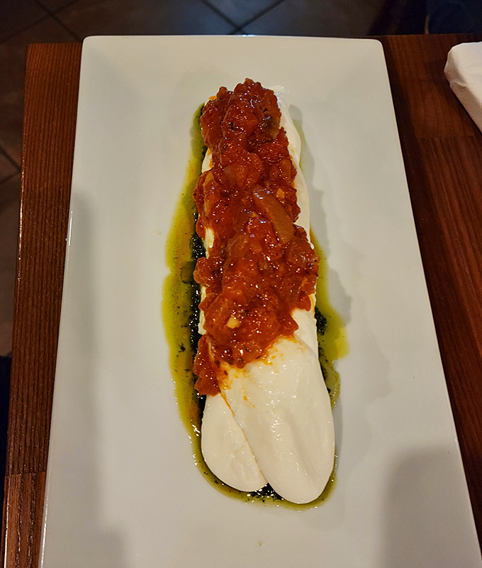 The Queso Trenza stretches dramatically across the plate, tomato sauce adding vibrant contrast. Cheese pulling a red carpet entrance worthy of applause.